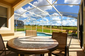 Um alpendre coberto com uma mesa redonda e cadeiras, piscina e vista para um campo de golfe.