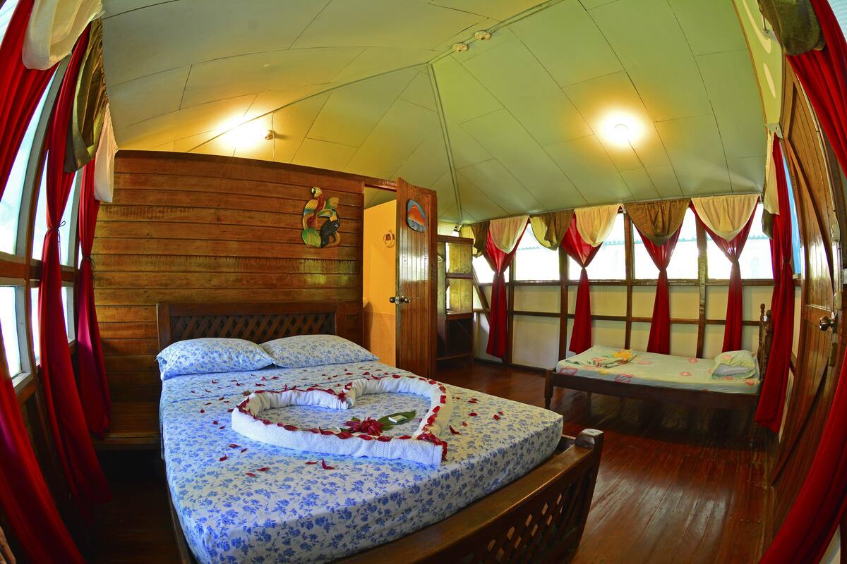 Quarto estilo cabana com interior de madeira, uma cama com roupa de cama florida e uma pequena mesa.