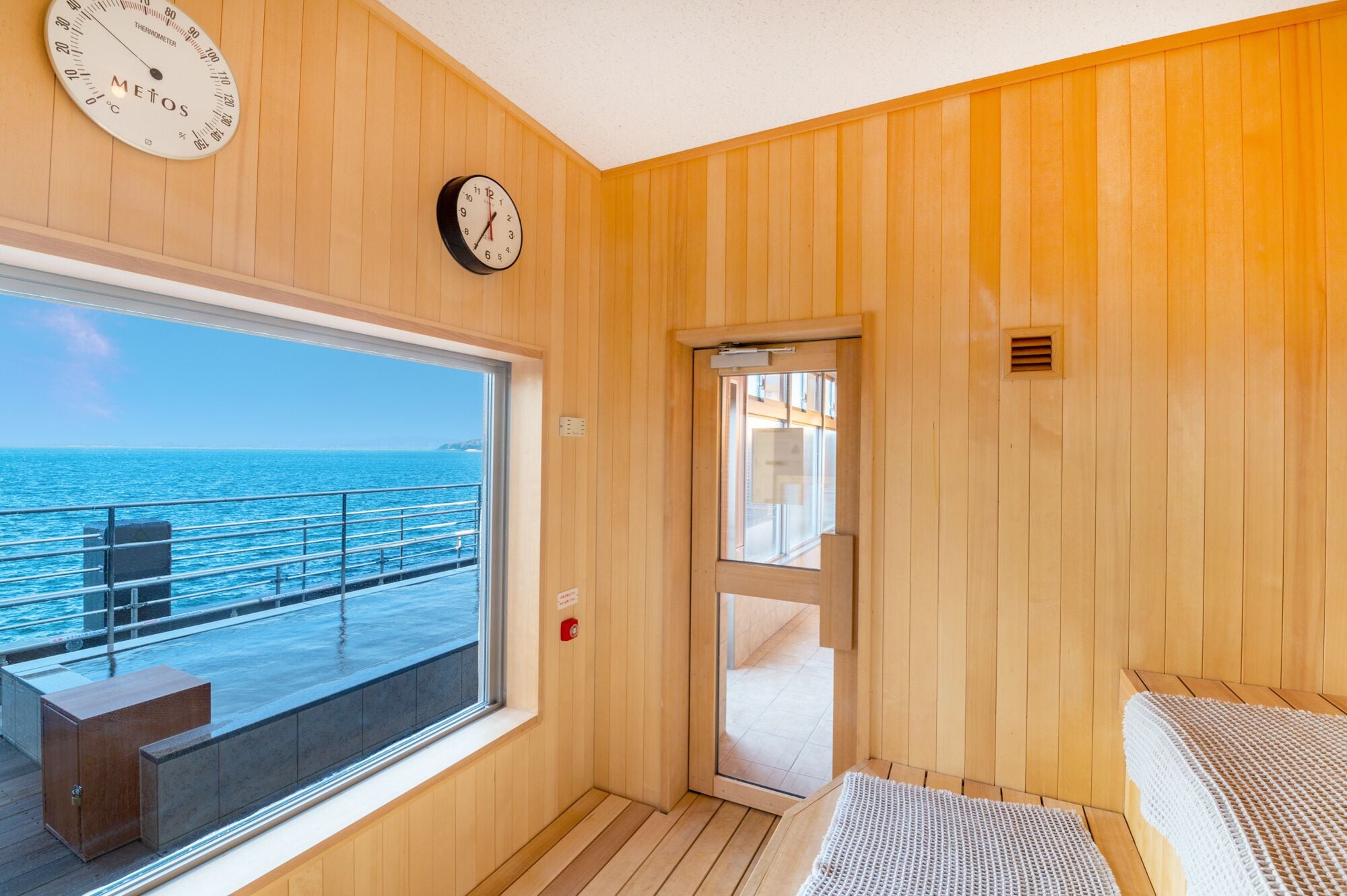Uma cabana de madeira com uma grande janela com vista para o mar, um termômetro e um relógio na parede.