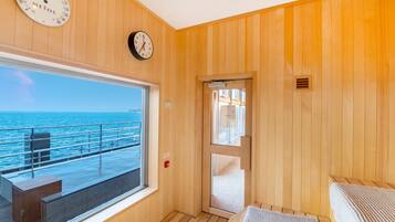 Uma cabana de madeira com uma grande janela com vista para o mar, um termômetro e um relógio na parede.