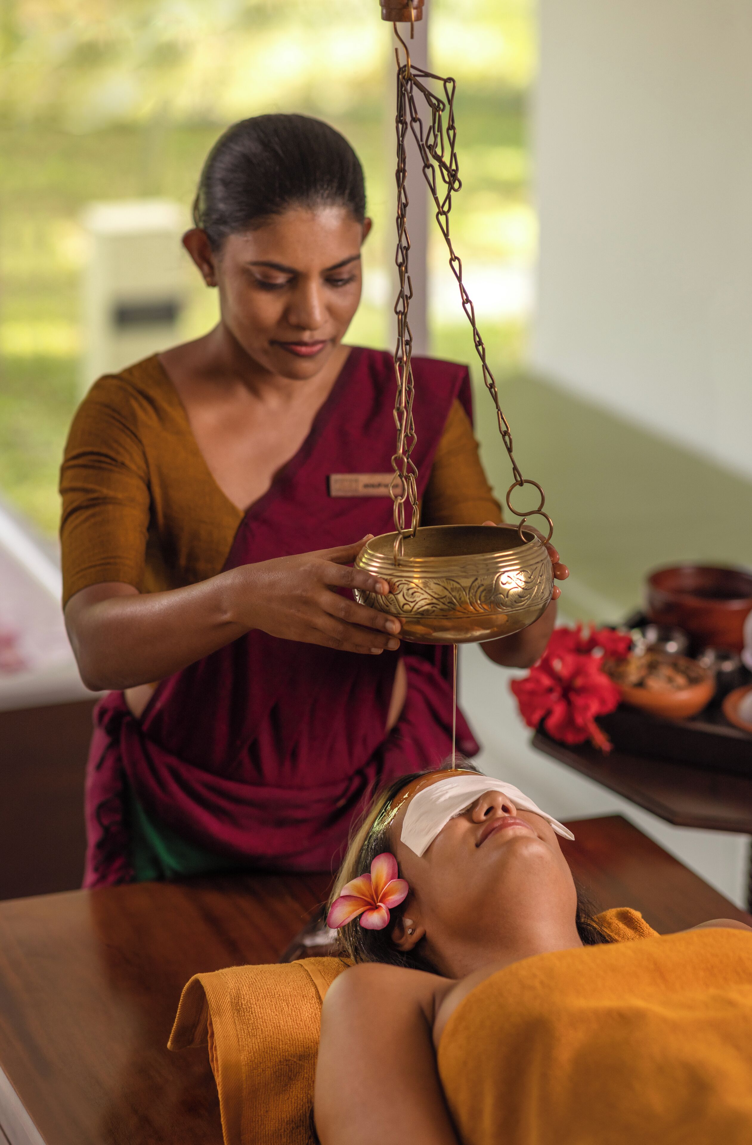 Uma pessoa recebendo massagem, com uma tigela e uma flor vermelha sobre a mesa.