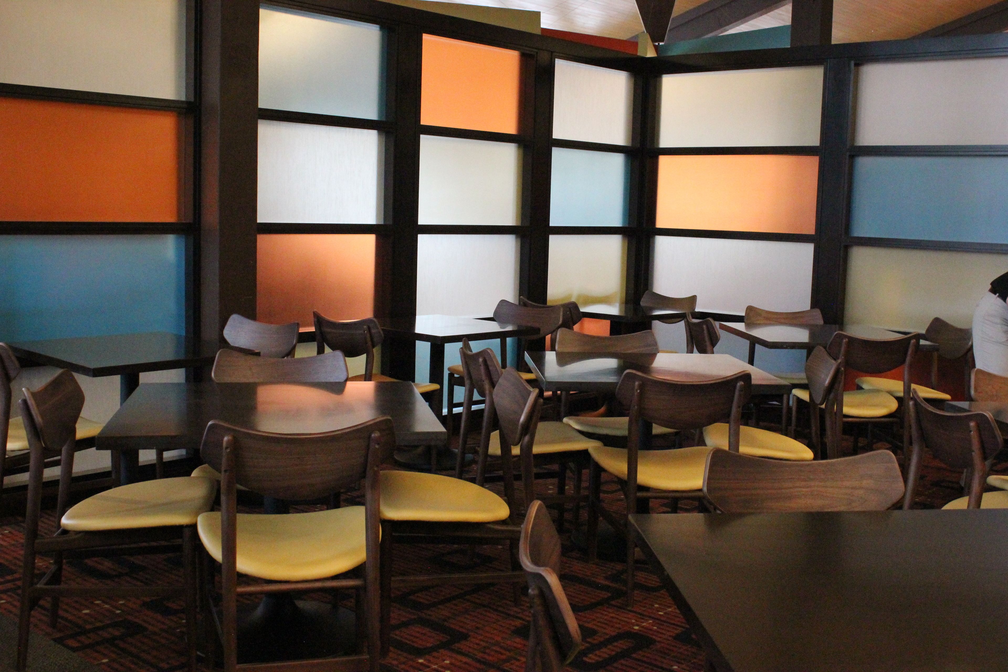 Um restaurante com várias mesas e cadeiras, algumas com almofadas amarelas.