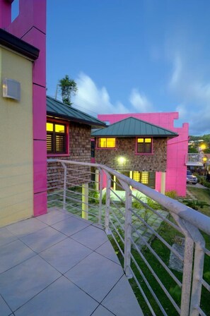 Um edifício moderno com paredes exteriores rosa e amarelo, um telhado verde e uma escadaria visível que leva a uma varanda.