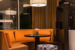 Um interior moderno com um sofá, uma mesa redonda com um vaso de flores e uma janela grande com cortinas.