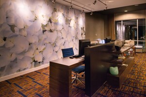 Uma área de recepção de hotel com design moderno, destacando um balcão grande, um computador e uma área de estar com uma cadeira azul.