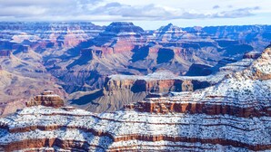 Ampla paisagem de cânion com formações rochosas estratificadas e neve.