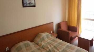 Quarto de hotel com cama, uma cadeira, um quadro na parede e janela com cortinas.