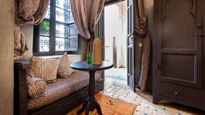 Quarto tradicional com um sofá estampado, uma mesa pequena com uma garrafa e um copo, e uma porta de madeira grande.