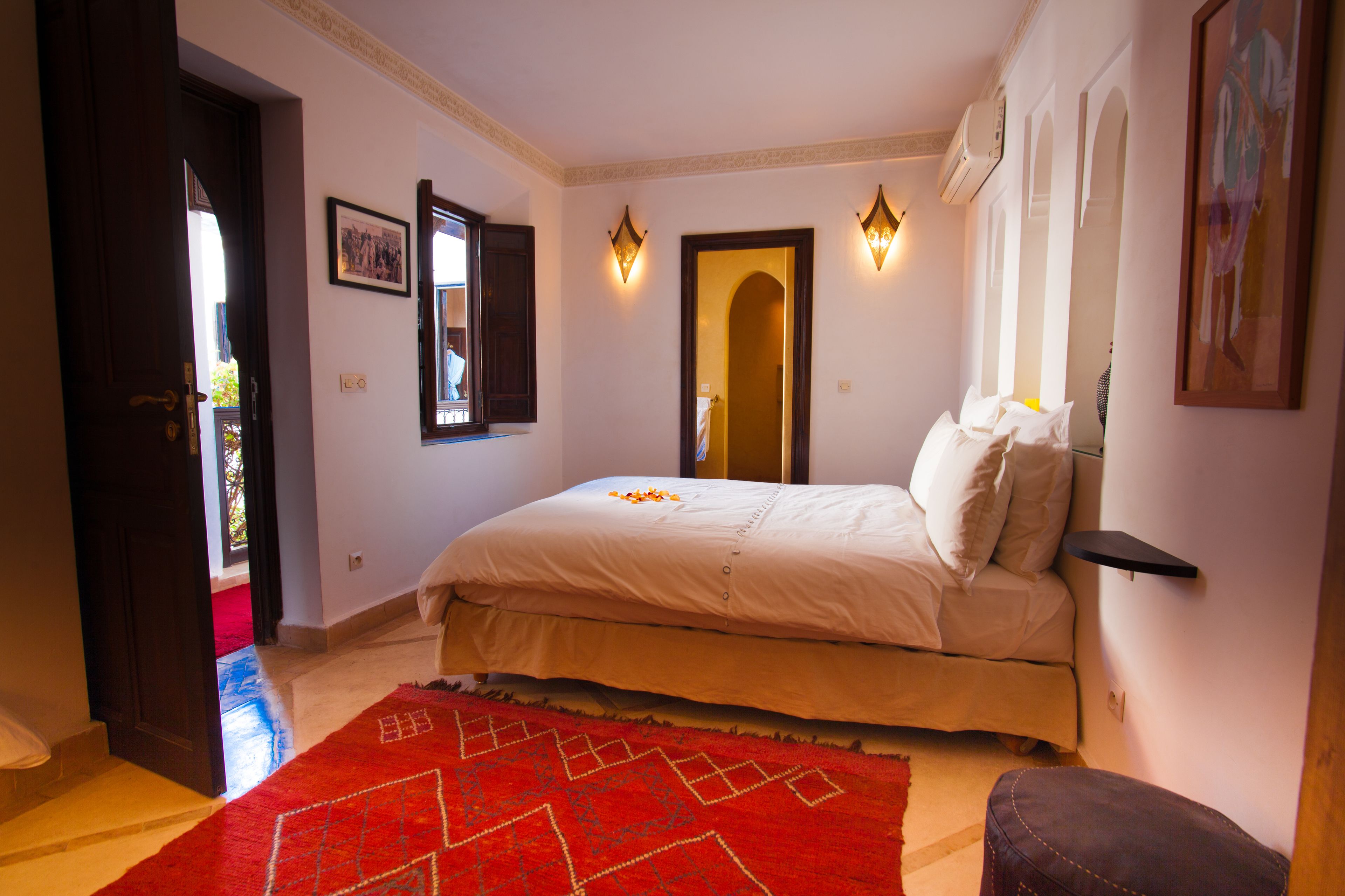Quarto com cama, tapete vermelho e porta para outro cômodo.