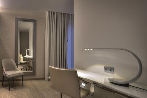Quarto de hotel moderno com escrivaninha, cadeira e um espelho grande.