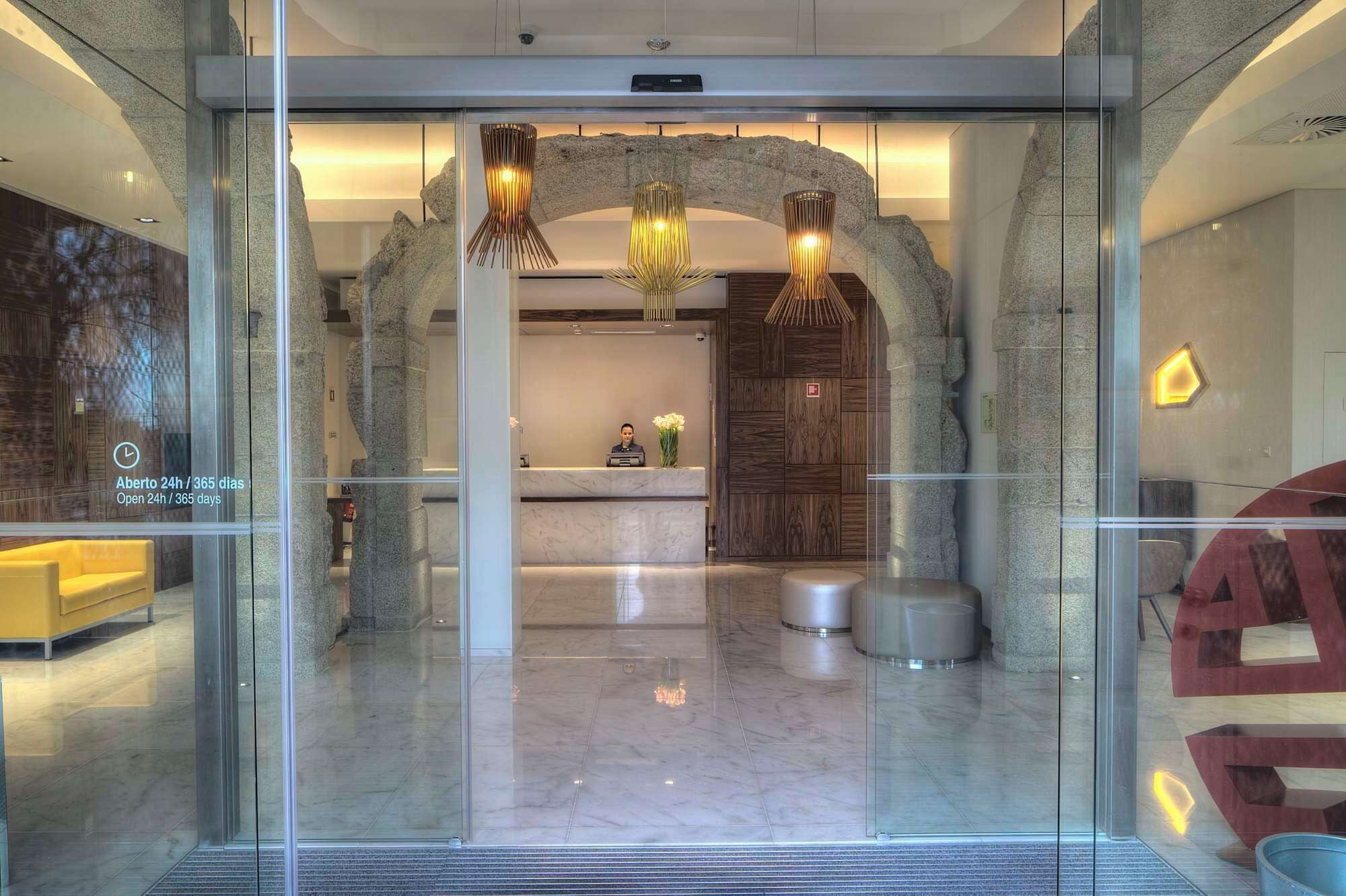 Um saguão moderno de hotel com uma mesa de recepção, um recepcionista e um arco de pedra.