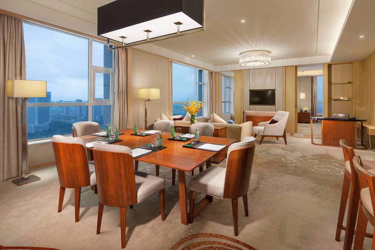 Uma sala de conferências de hotel com uma mesa grande, cadeiras, uma TV e vista para a cidade.