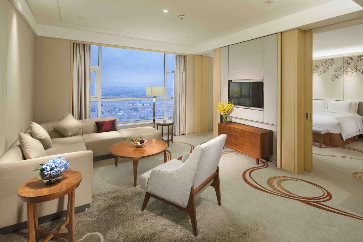 Quarto de hotel com sofá, poltrona, mesa de centro, TV e uma cama com vista para a cidade.