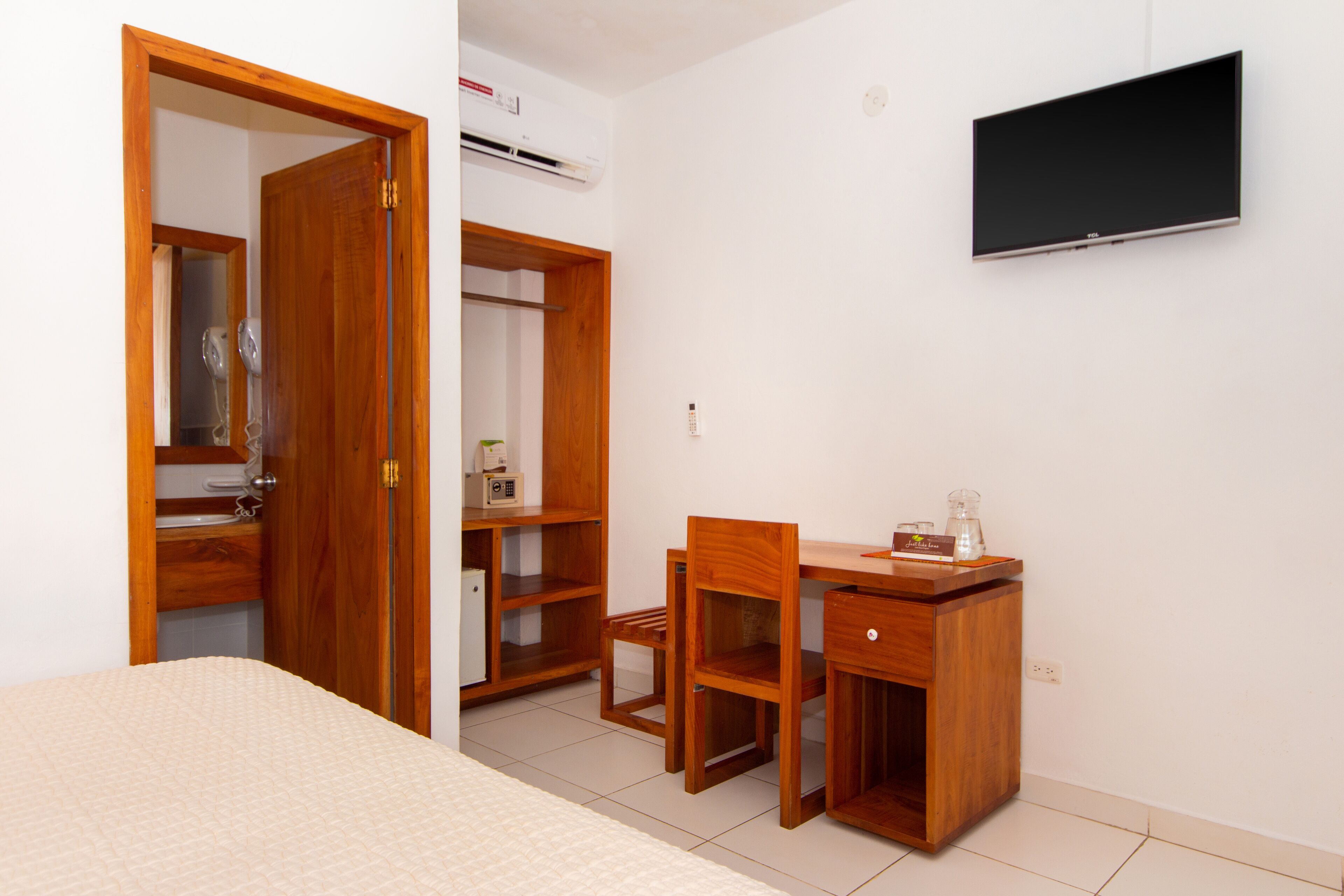 Quarto com guarda-roupa de madeira, escrivaninha com cadeira, cama e televisão montada na parede.