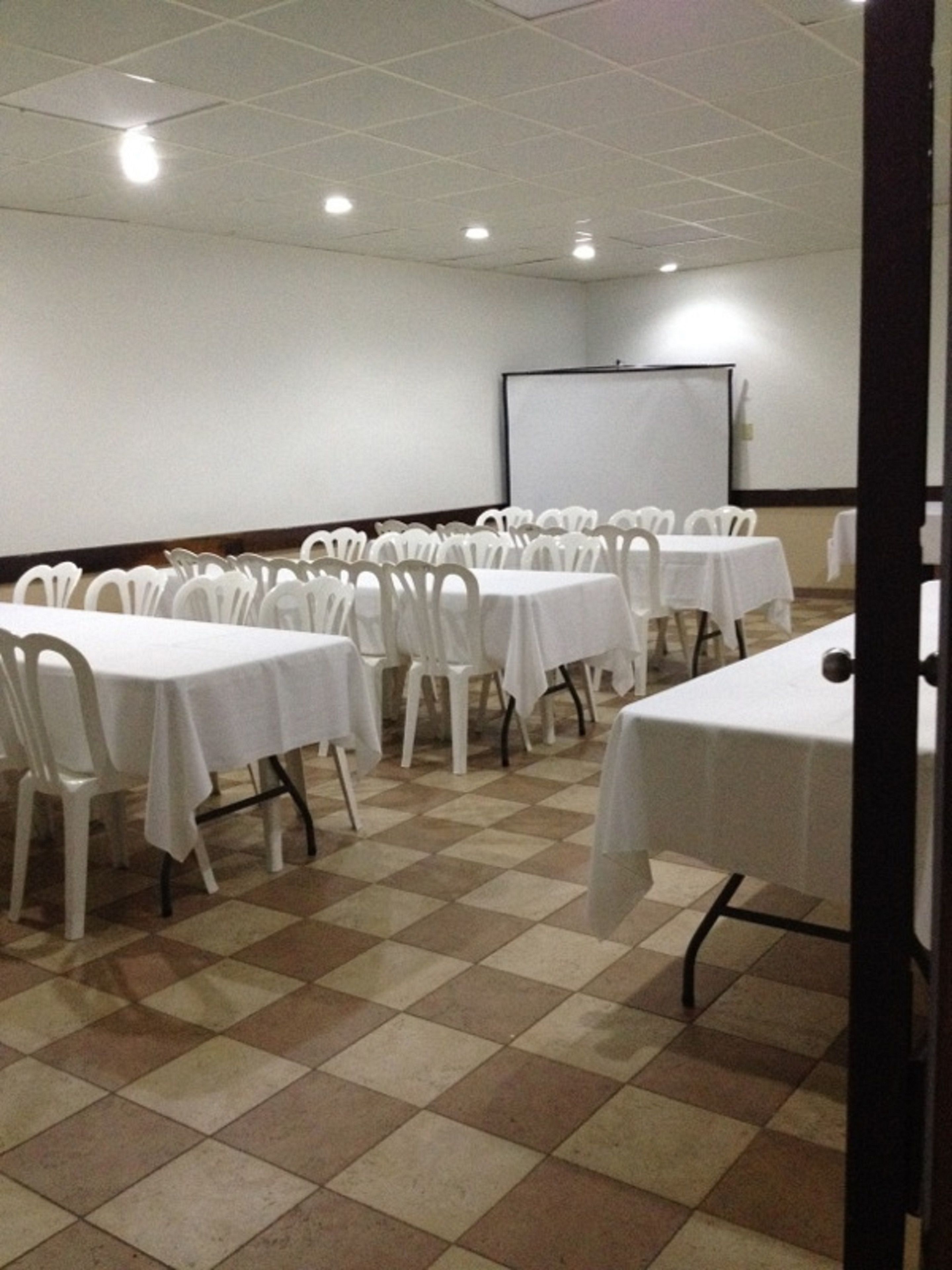 Uma sala de conferências com várias mesas e cadeiras, um quadro branco e uma tela de projeção.