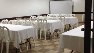 Uma sala de conferências com várias mesas e cadeiras, um quadro branco e uma tela de projeção.