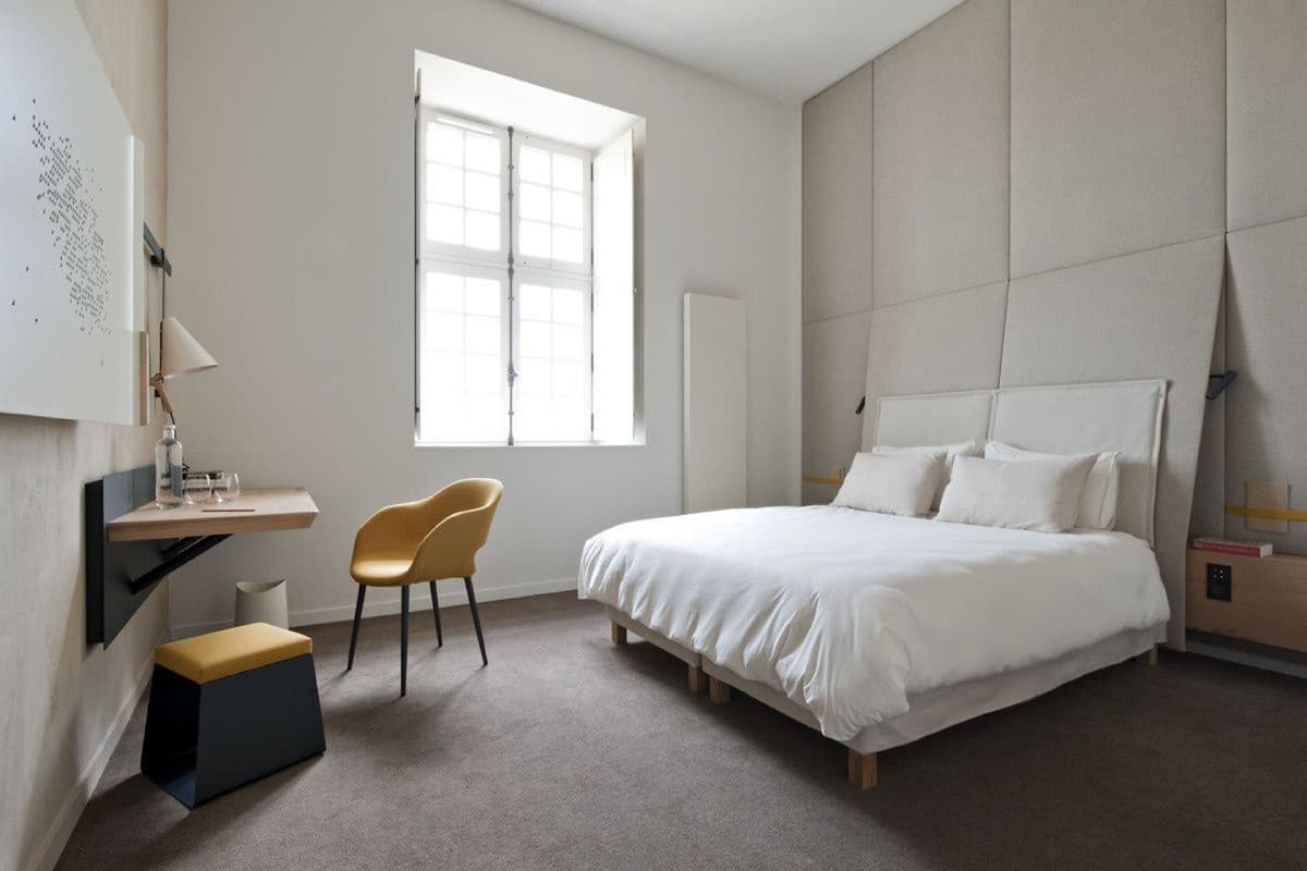Quarto moderno com uma cama grande, uma escrivaninha com cadeira e uma janela que ilumina naturalmente o espaço.