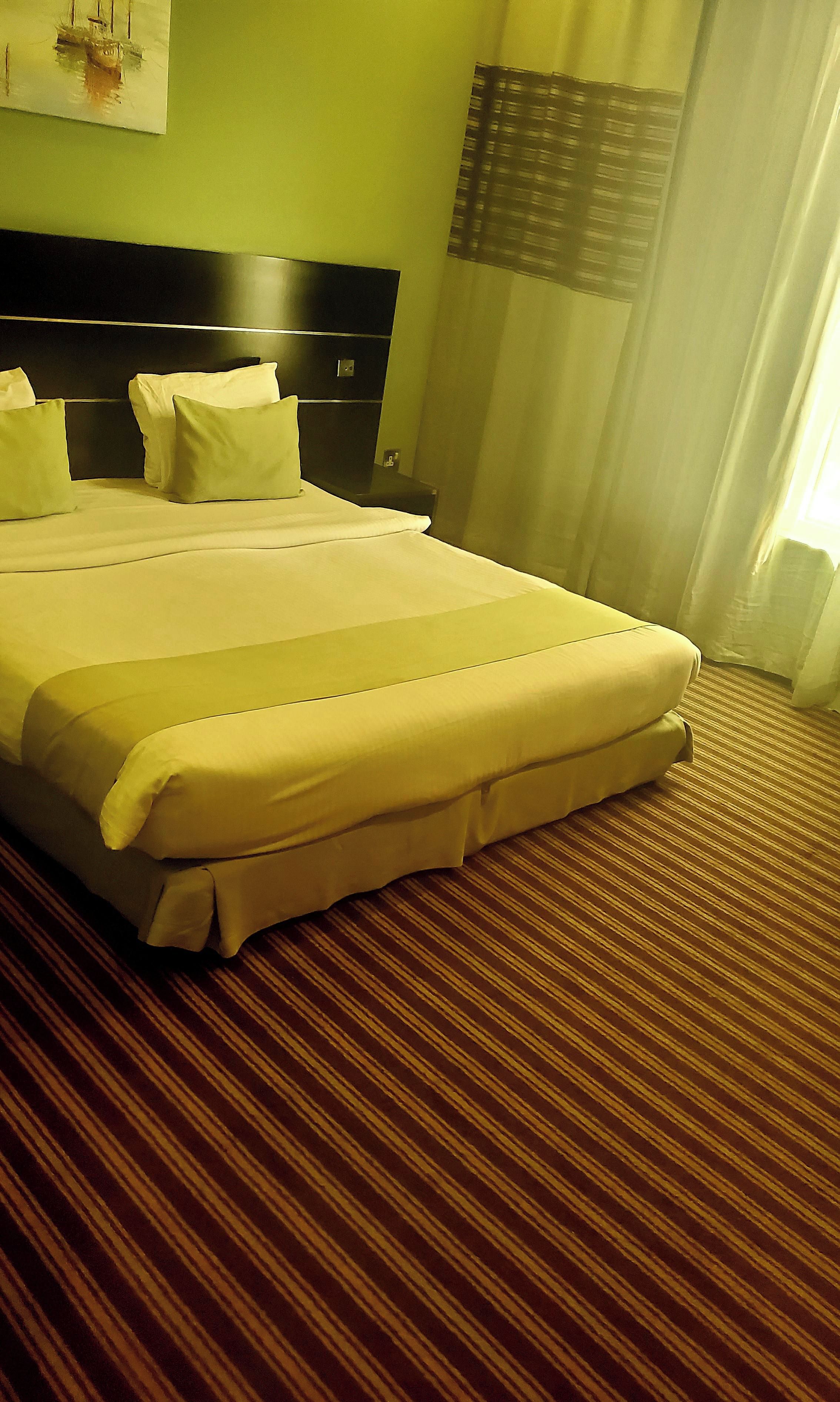 Quarto de hotel com uma cama grande, cabeceira e tapete listrado.