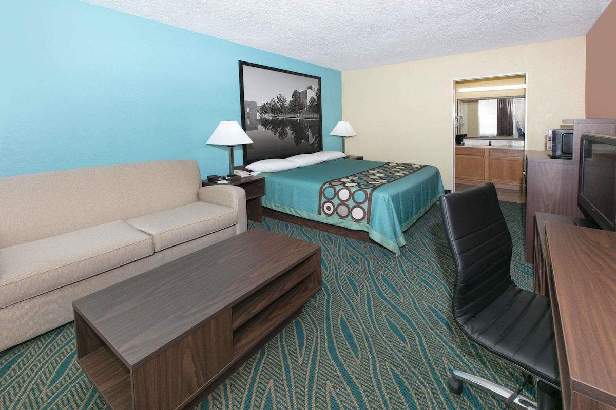 Quarto de hotel com cama, sofá, escrivaninha, cadeira e cozinha compacta.
