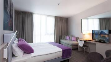 Quarto de hotel com cama, escrivaninha, cadeira, sofá e televisão.