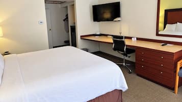 Quarto de hotel com cama, escrivaninha, cadeira, televisão e espelho.