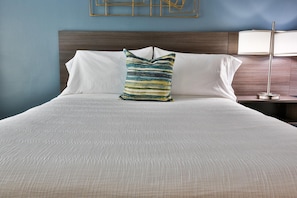 Cama bem arrumada com travesseiro listrado, cabeceira de madeira e mesa de cabeceira com abajur.