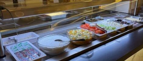 Uma área de buffet com diversas opções de comida, bancada de mármore e certificados emoldurados na parede.