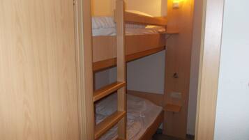 Quarto com beliches de madeira, uma porta com interruptor de luz e um pequeno prateleira.