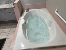 Uma banheira com água corrente, chão de azulejos e um canto da parede com acabamento rosa.