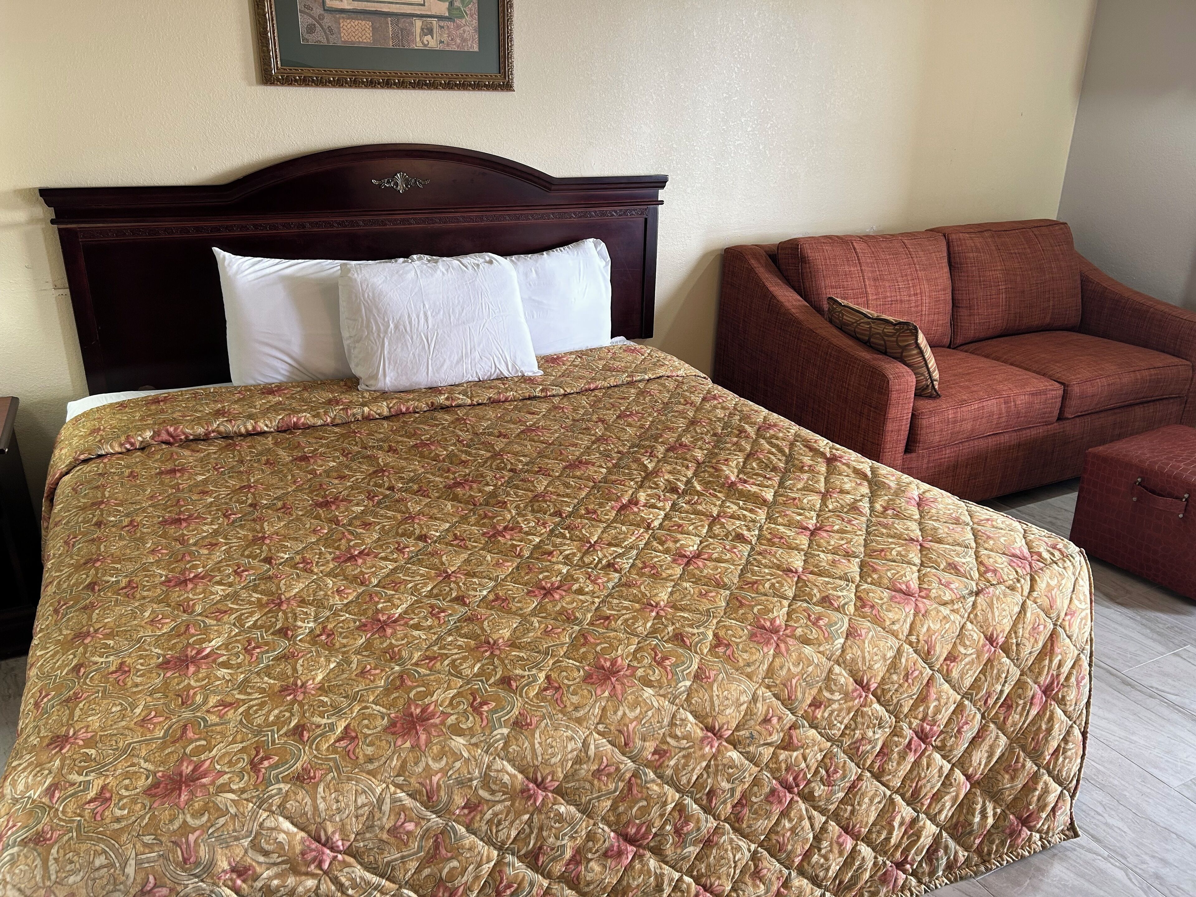 Quarto de hotel com uma cama grande, cabeceira de madeira, poltrona vermelha e um quadro pendurado na parede.
