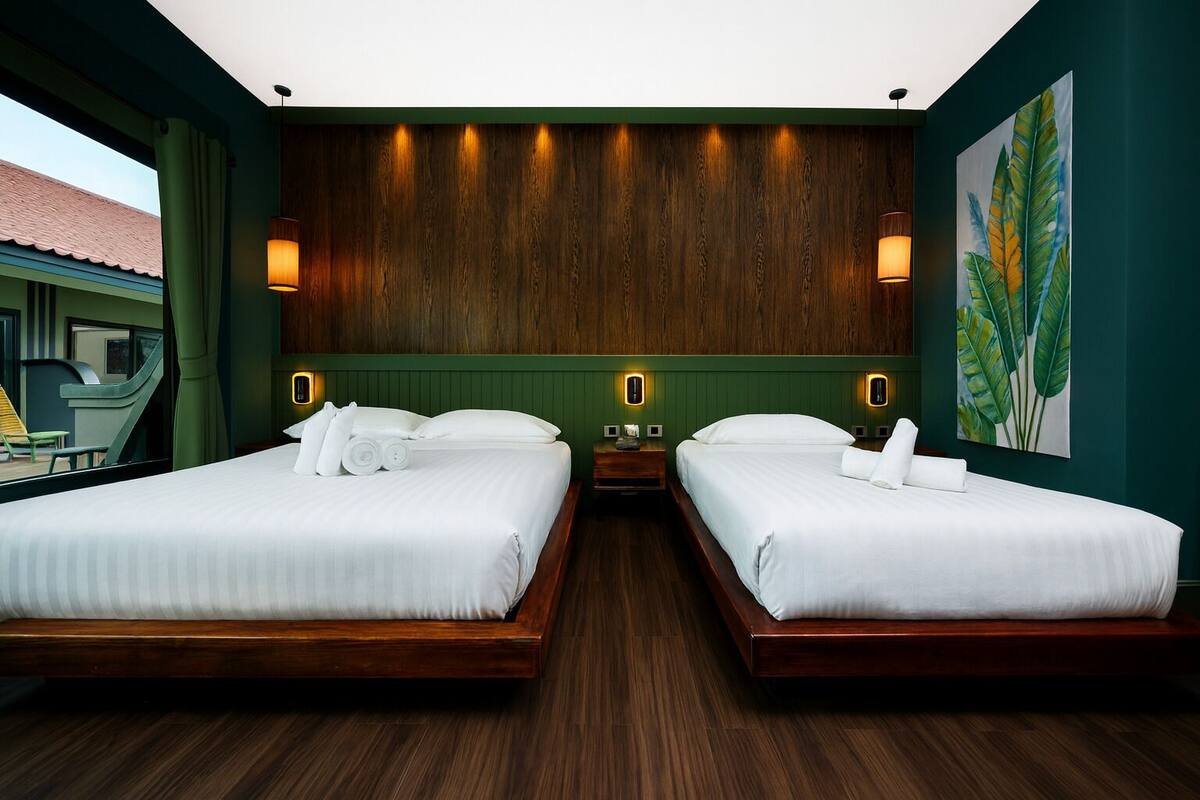Quarto de hotel com duas camas, cabeceira de madeira, paredes verdes e uma janela grande com vista para um edifício.