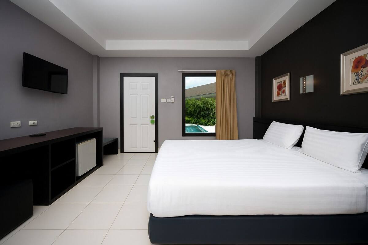 Quarto de hotel moderno com uma cama grande, televisão de tela plana na parede, escrivaninha com cadeira e porta para uma varanda com vista para a piscina.