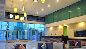 Um lobby moderno com sofás de vime, um balcão de recepção e amplas janelas com vista para a paisagem urbana.