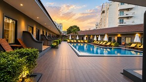 Uma área na piscina com espreguiçadeiras e guarda-sóis, céu claro e edifícios ao fundo.