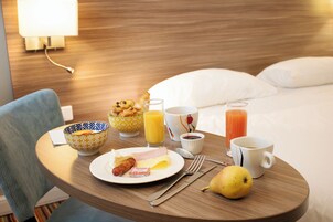 Uma mesa de café da manhã com croissants, suco de laranja, um copo de suco de laranja, uma xícara de café, um prato com ovos, presunto e uma pêra.