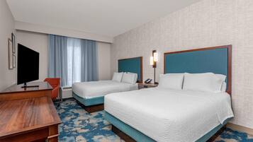 Quarto de hotel com duas camas, uma escrivaninha, uma televisão e uma janela com cortinas.