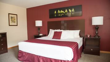 Quarto de hotel com uma cama grande, duas mesas de cabeceira, um criado-mudo, um quadro na parede e uma fotografia emoldurada na parede.