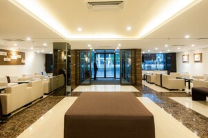 Um saguão de hotel com área de estar central, balcão de recepção e entrada de vidro.