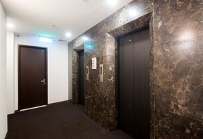 Corredor com dois elevadores, paredes de mármore e piso coberto por carpete.