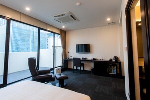 Quarto de hotel com cama, escrivaninha, cadeira, televisão e minibar.