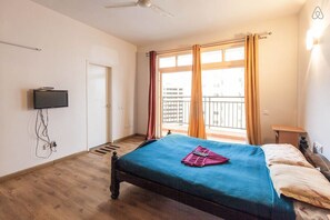 Quarto com cama, televisão na parede, janela com cortinas e varanda.