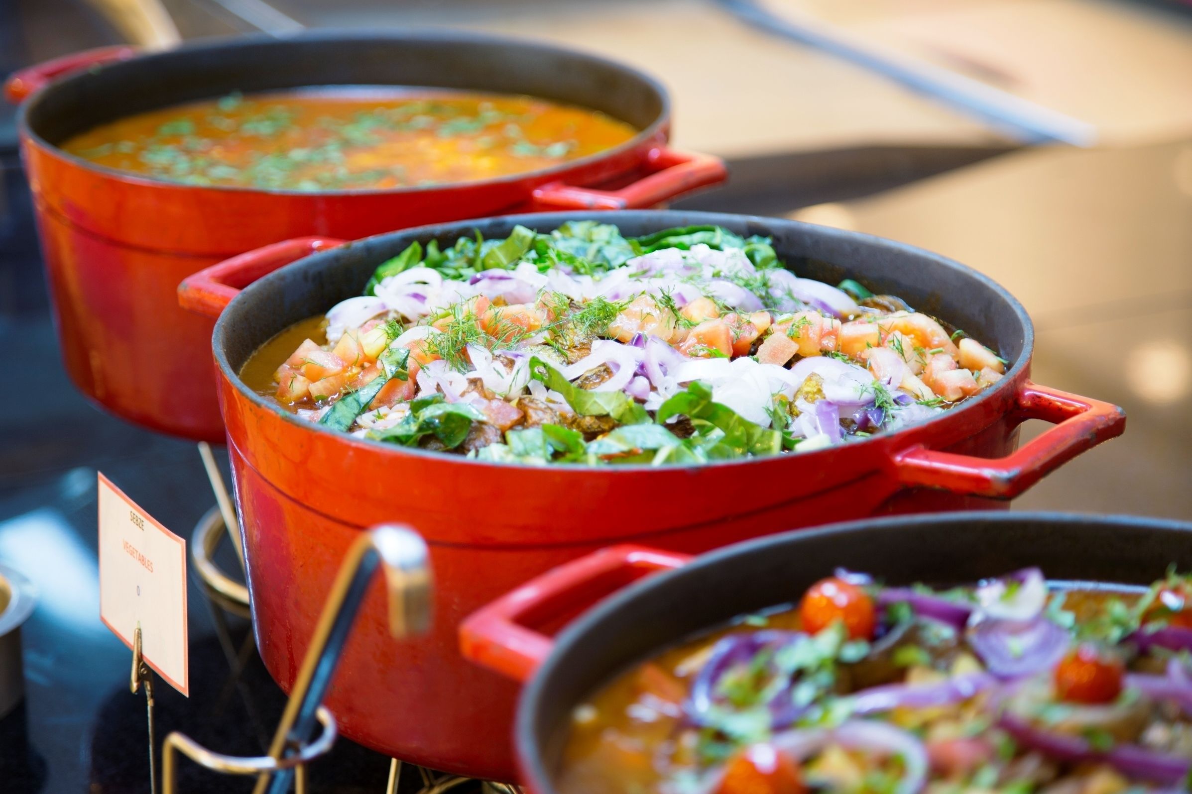 Três panelas vermelhas com comida, uma com salada e as outras com sopa.