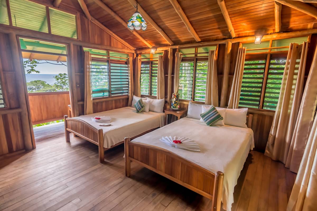 Uma cabana de madeira com duas camas, piso de madeira e janelas amplas com cortinas.