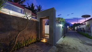Uma passagem que leva a uma casa, com um muro de pedra de um lado e uma antena parabólica do outro.