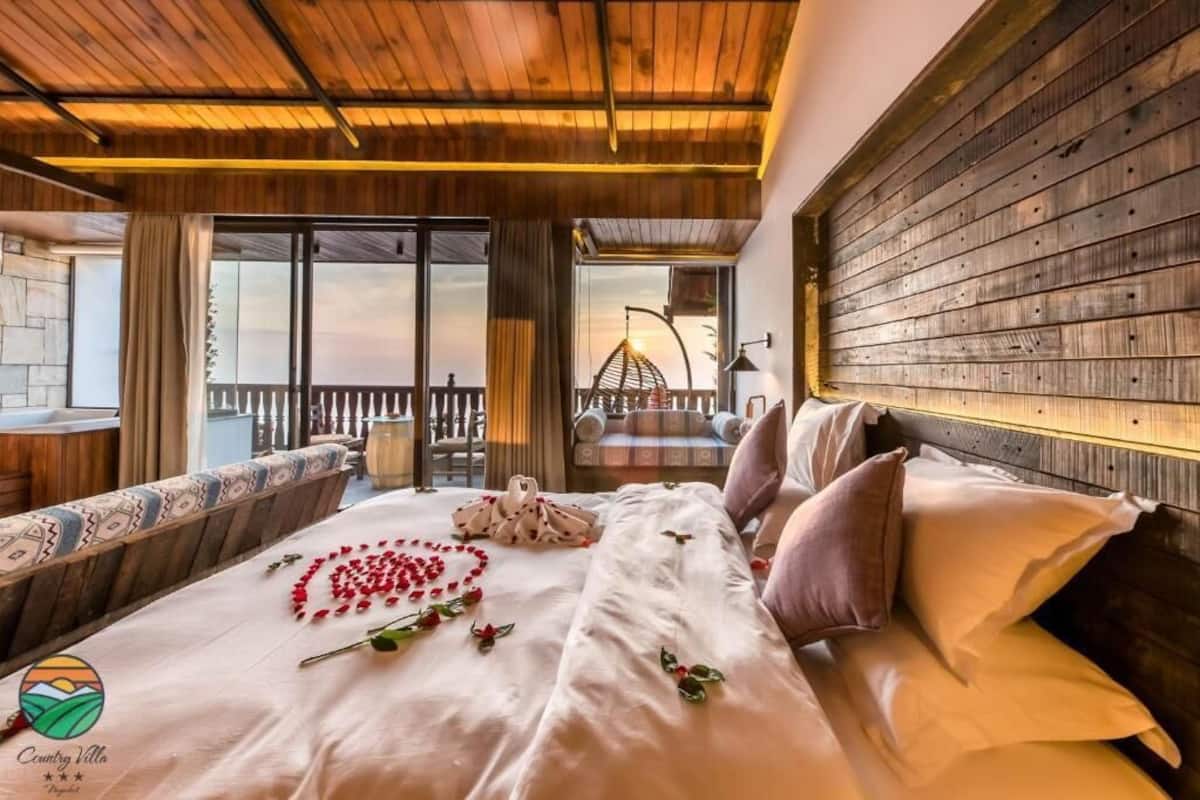 Quarto com teto de madeira, cama com roupa de cama branca, varanda com vista e parede de madeira.