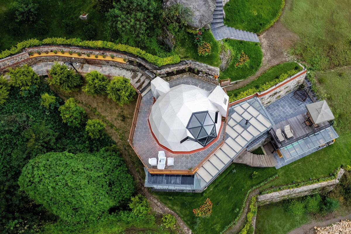 Vista aérea de um edifício moderno e circular, com cobertura de vidro, cercado por vegetação exuberante e um caminho de pedra.