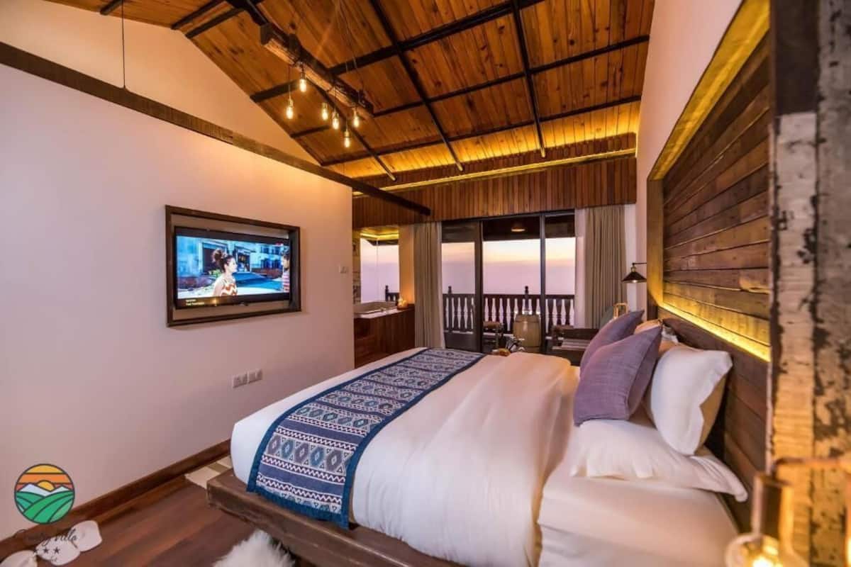 Quarto com cama, televisão na parede, teto de madeira e varanda com vista.
