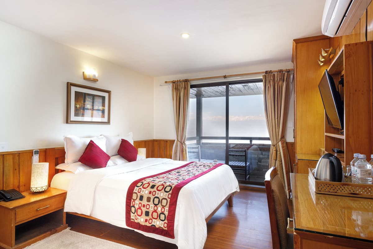 Quarto de hotel com uma cama grande, mesa de cabeceira com abajur, televisão e vista para o exterior.