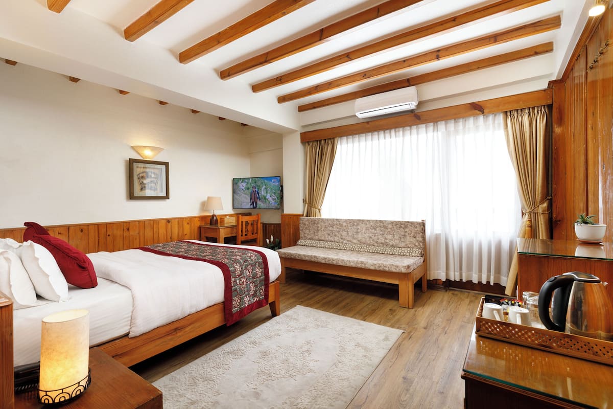 Quarto de hotel com uma cama de madeira, um sofá, uma escrivaninha e uma televisão.