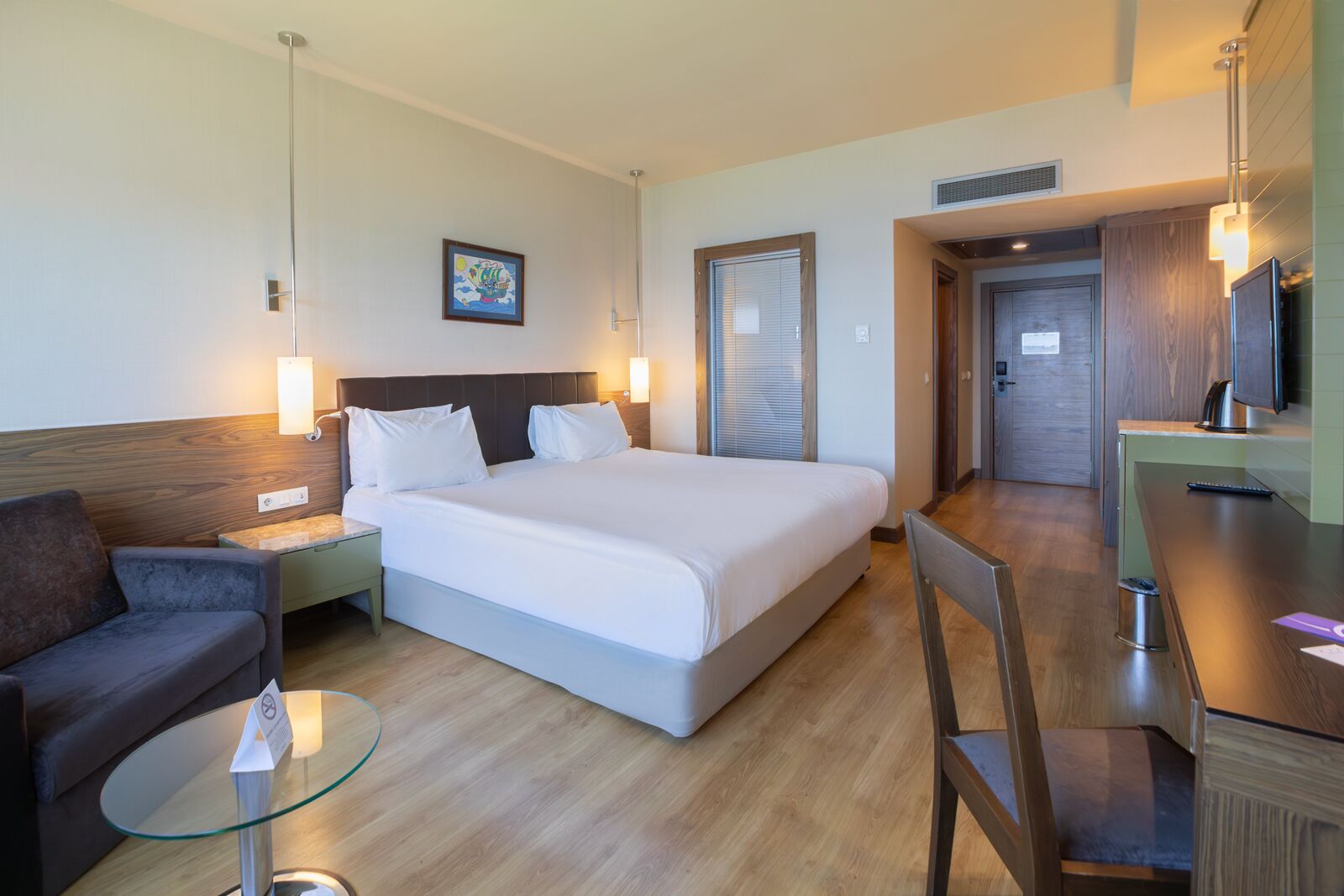 Quarto de hotel com cama, escrivaninha, cadeira, sofá e televisão.